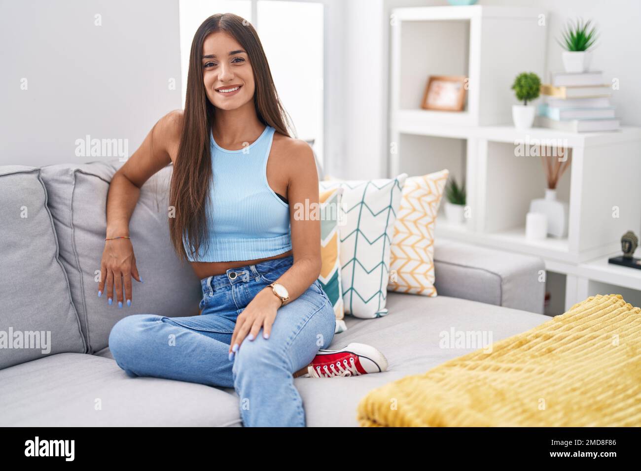 Young brunette woman sitting on the sofa at home with a happy and cool ...