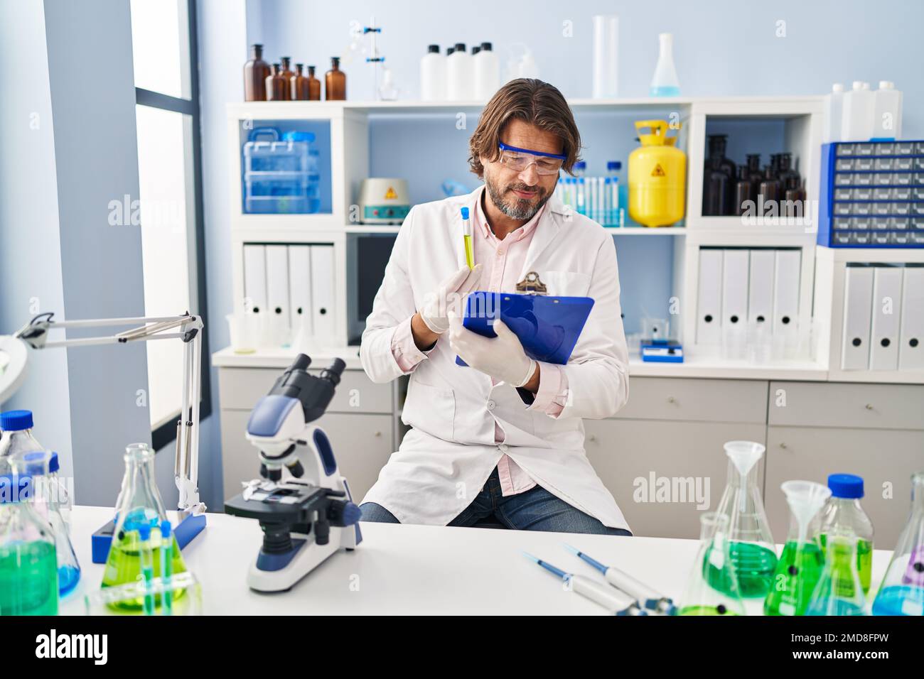 Middle age man scientist holding test tube reading document at ...