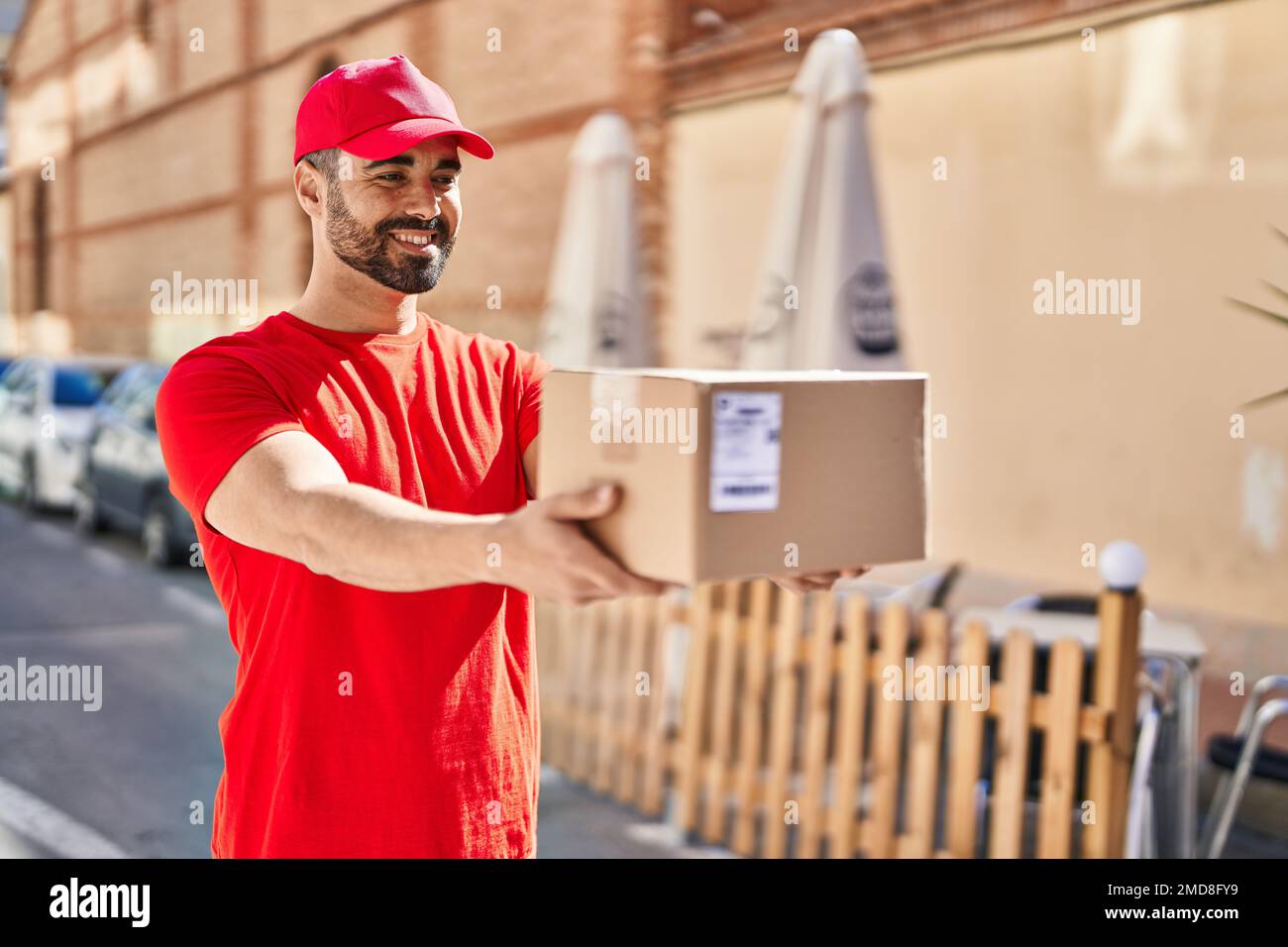 Young hispanic man courier holding package at street Stock Photo - Alamy