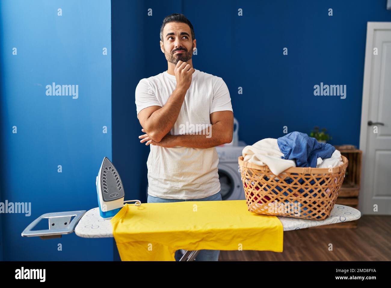 Young hispanic man with beard ironing clothes at home thinking ...