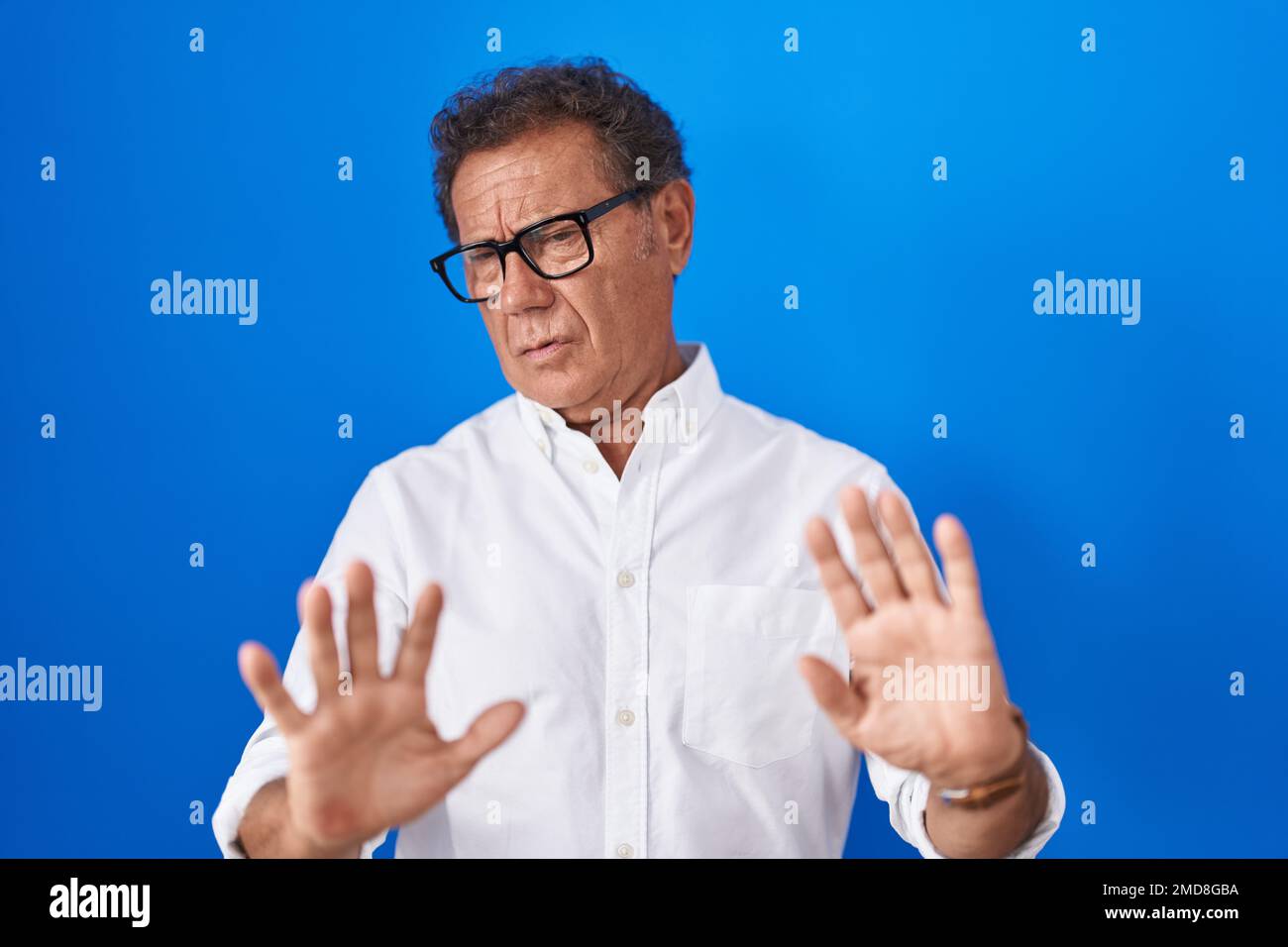Middle age hispanic man standing over blue background moving away hands ...