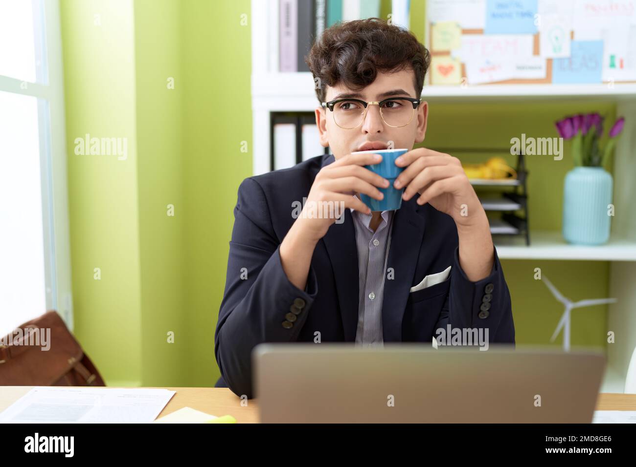 Non binary man business worker using laptop drinking coffee at office ...