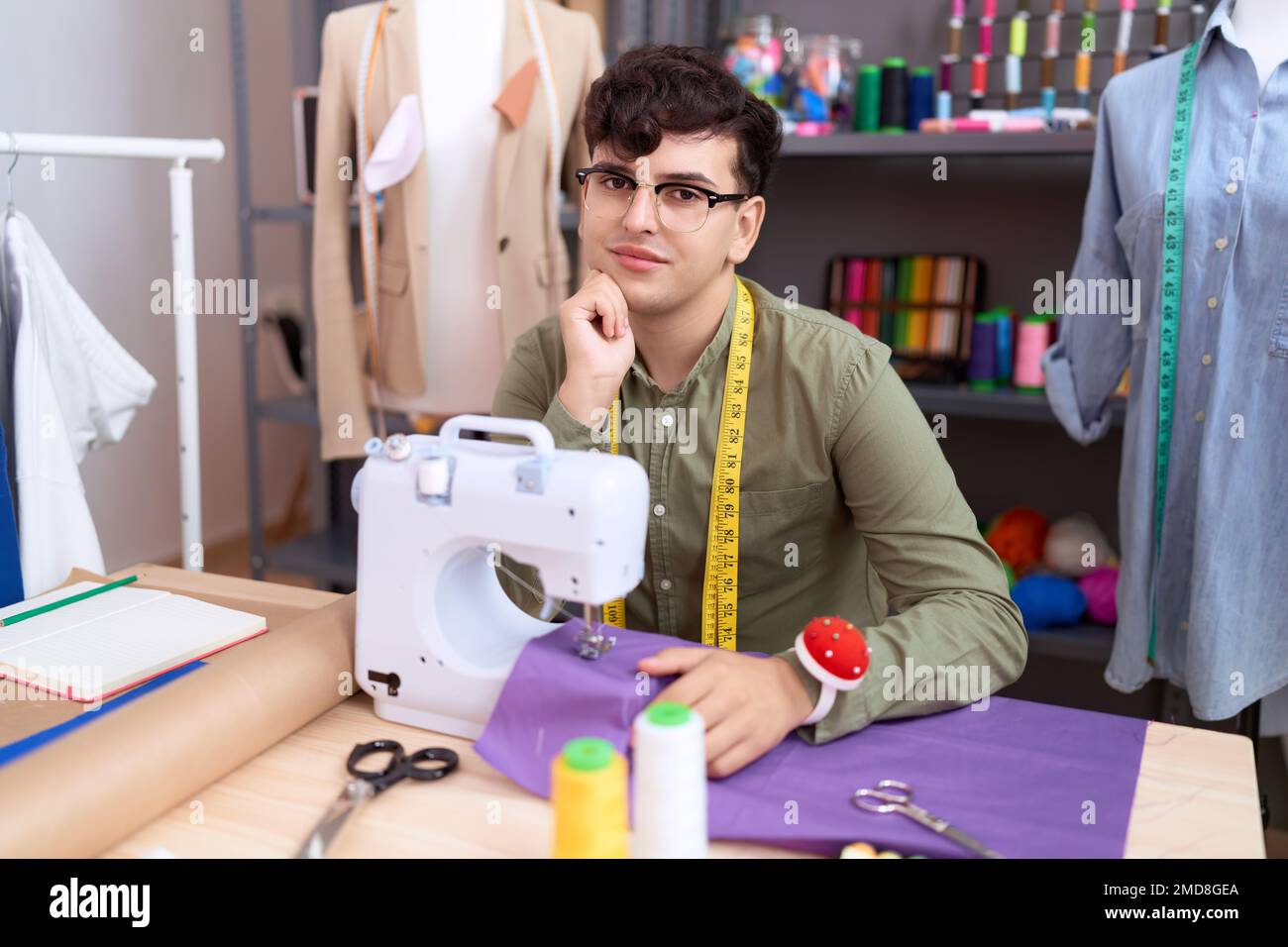 Non binary man tailor smiling confident sitting on table at atelier ...