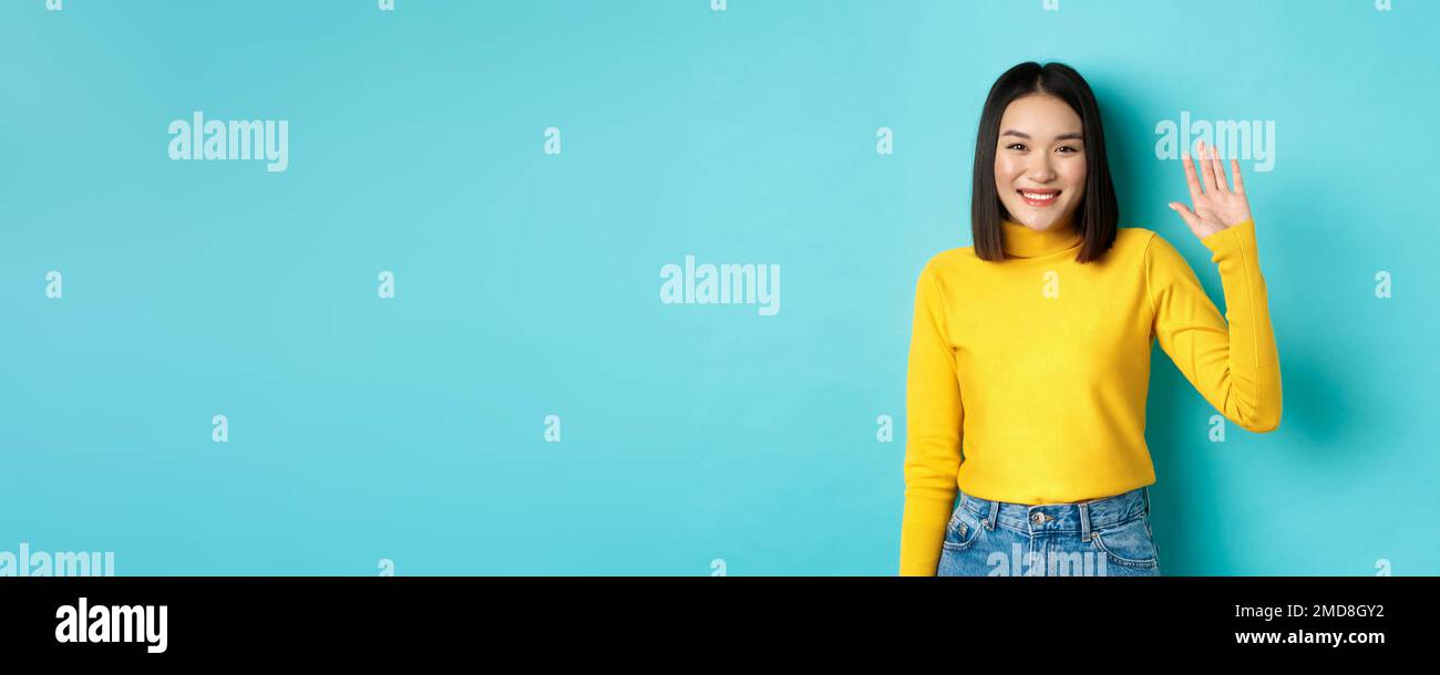 Portrait of beautiful asian girl with happy smile, waving hand to say ...