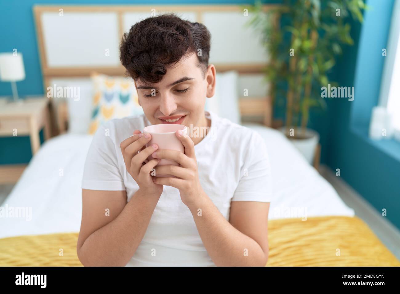 Non binary man drinking cup of coffee sitting on bed at bedroom Stock ...
