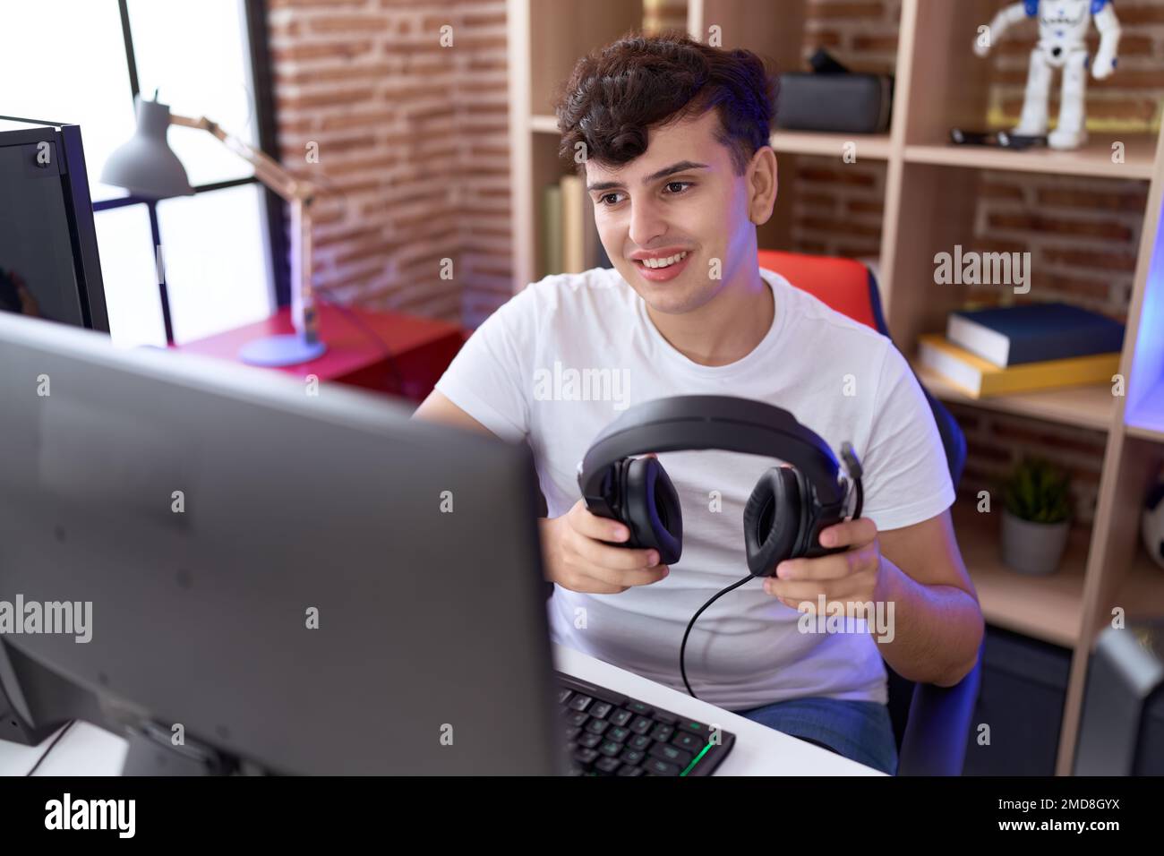 Non binary man streamer sitting on table holding headphones at gaming ...