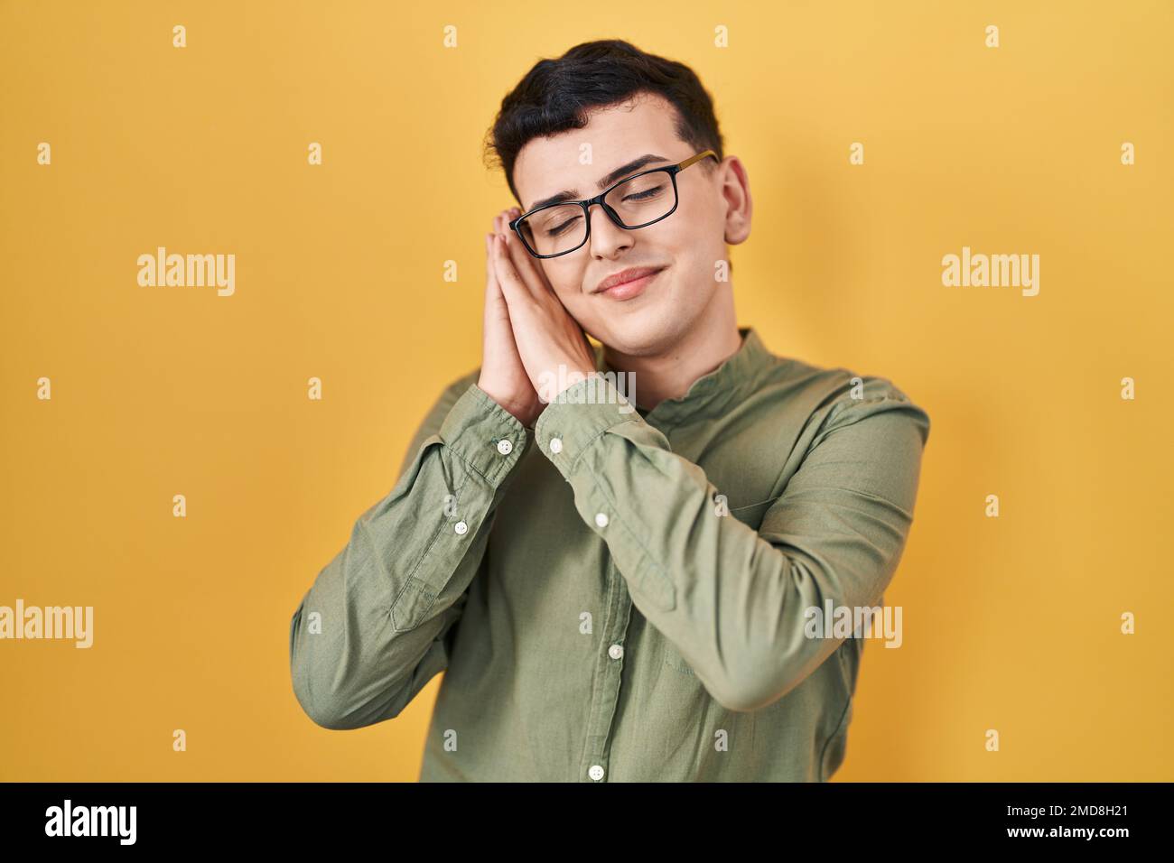 Non binary person standing over yellow background sleeping tired ...