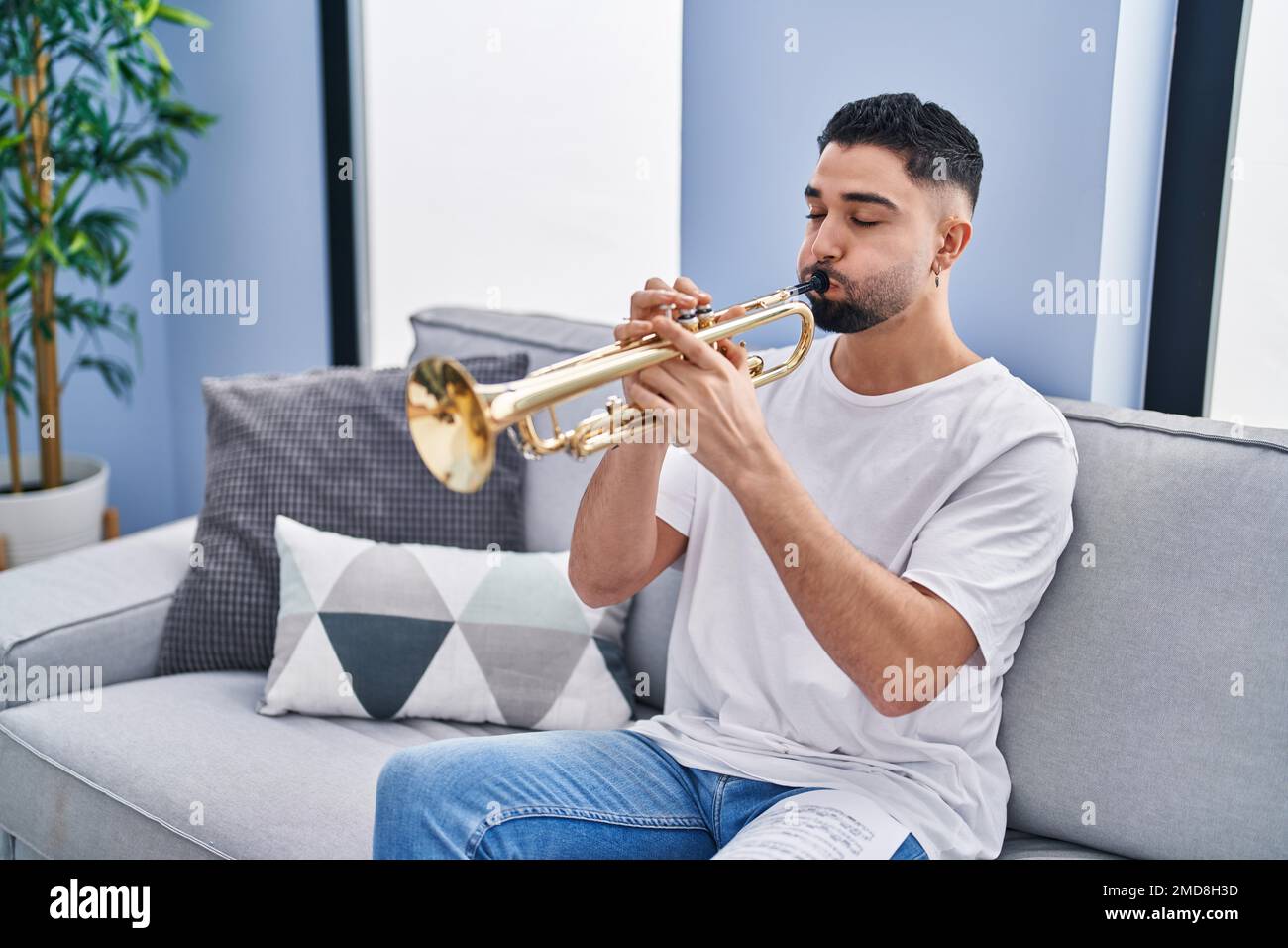Young arab man musician playing trumpet sitting on sofa at home Stock ...