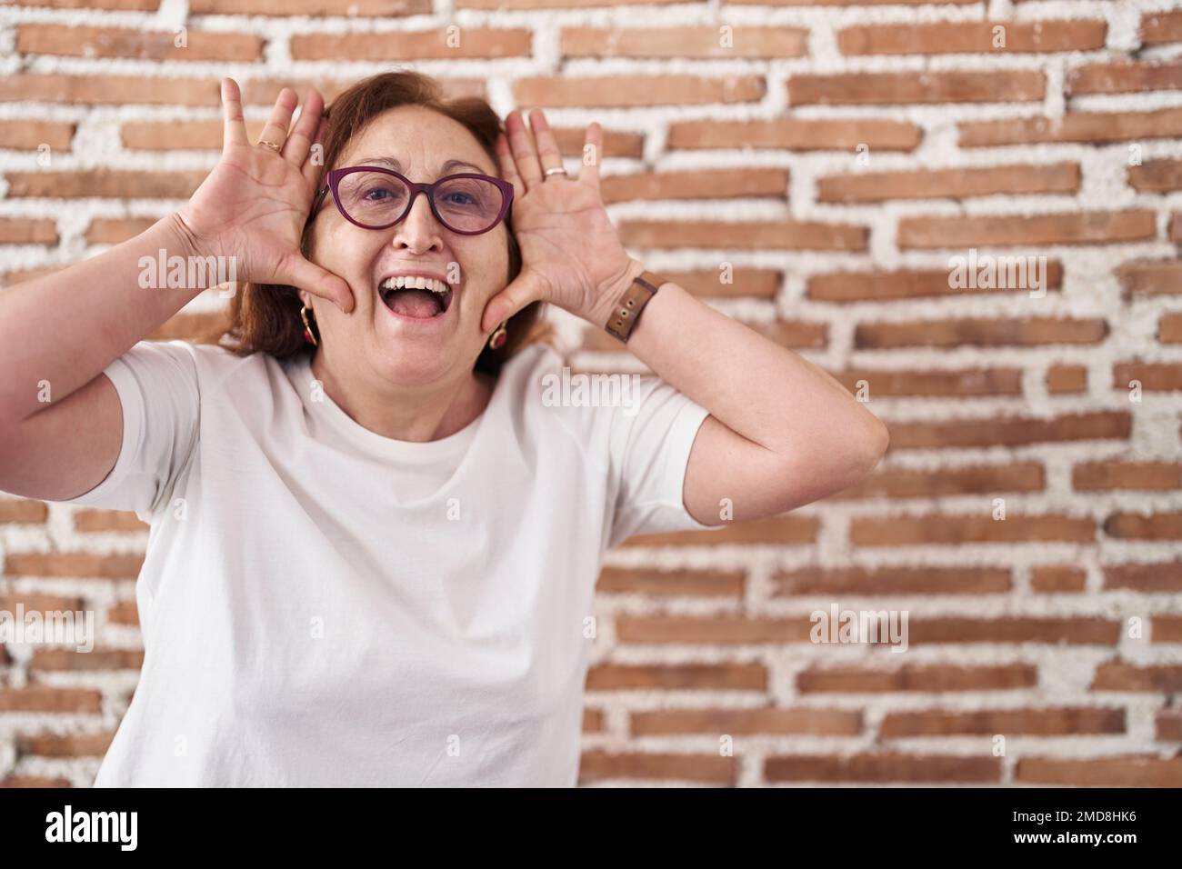 Senior woman with glasses standing over bricks wall smiling cheerful ...