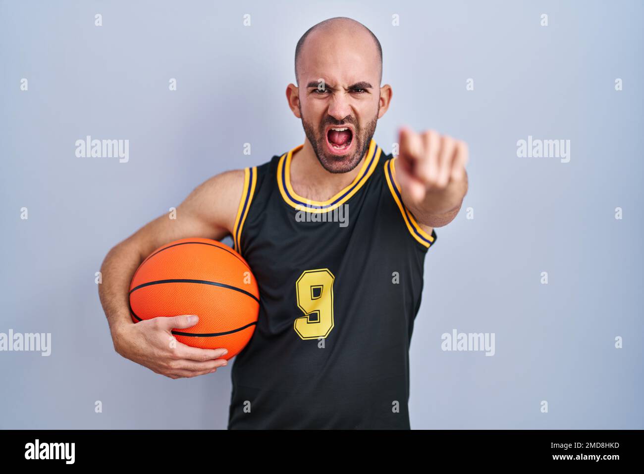 Young bald man with beard wearing basketball uniform holding ball ...