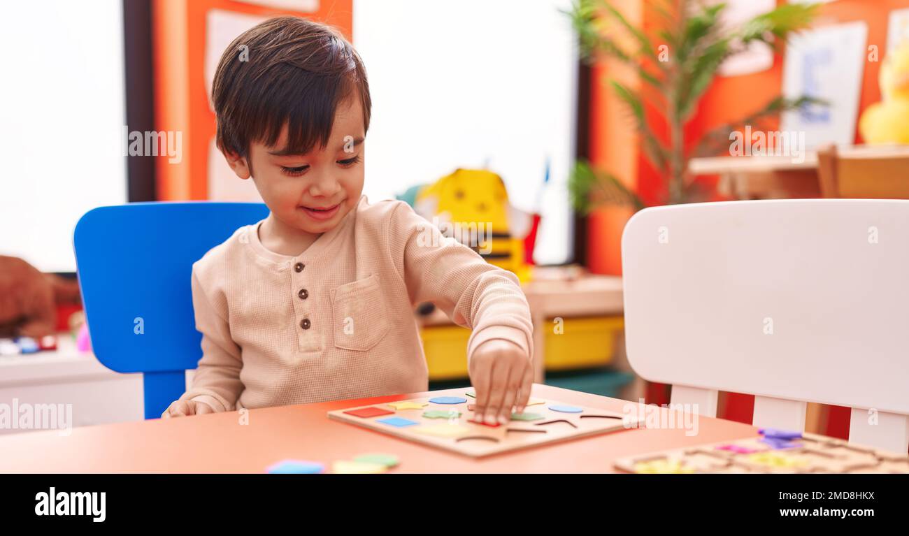 Adorable hispanic boy playing with maths puzzle game sitting on table ...