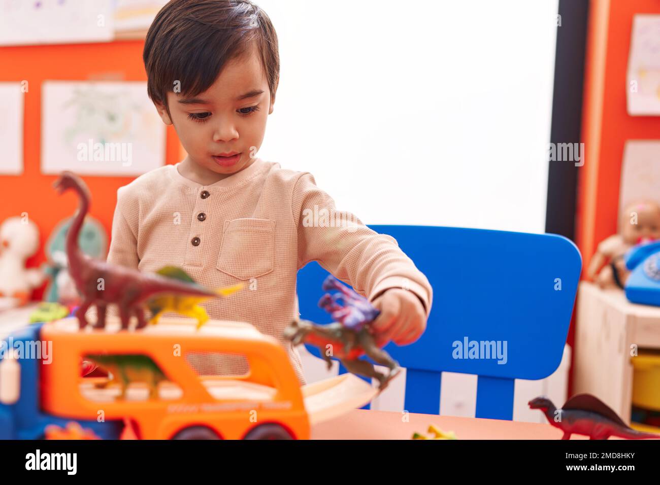 Adorable hispanic boy playing with cars and dino toys standing at ...