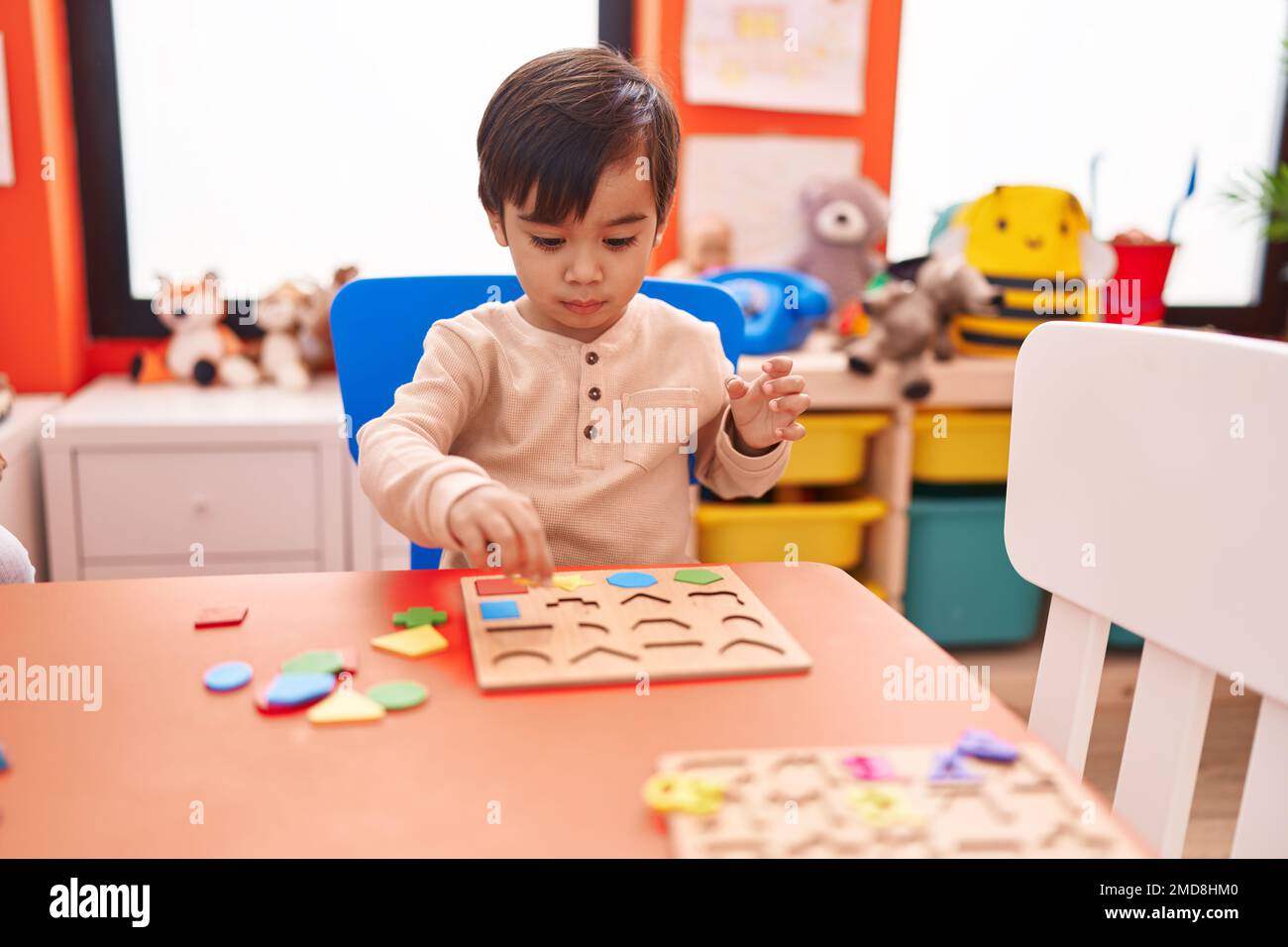 Adorable hispanic boy playing with maths puzzle game sitting on table ...