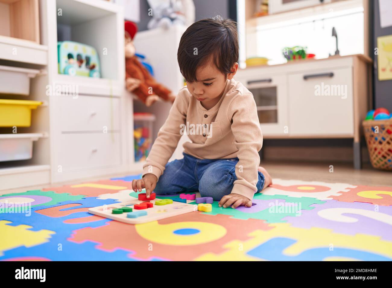 Adorable hispanic boy playing with maths puzzle game sitting on floor ...
