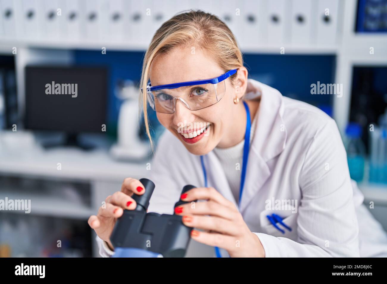 Young blonde woman scientist smiling confident using microscope at ...