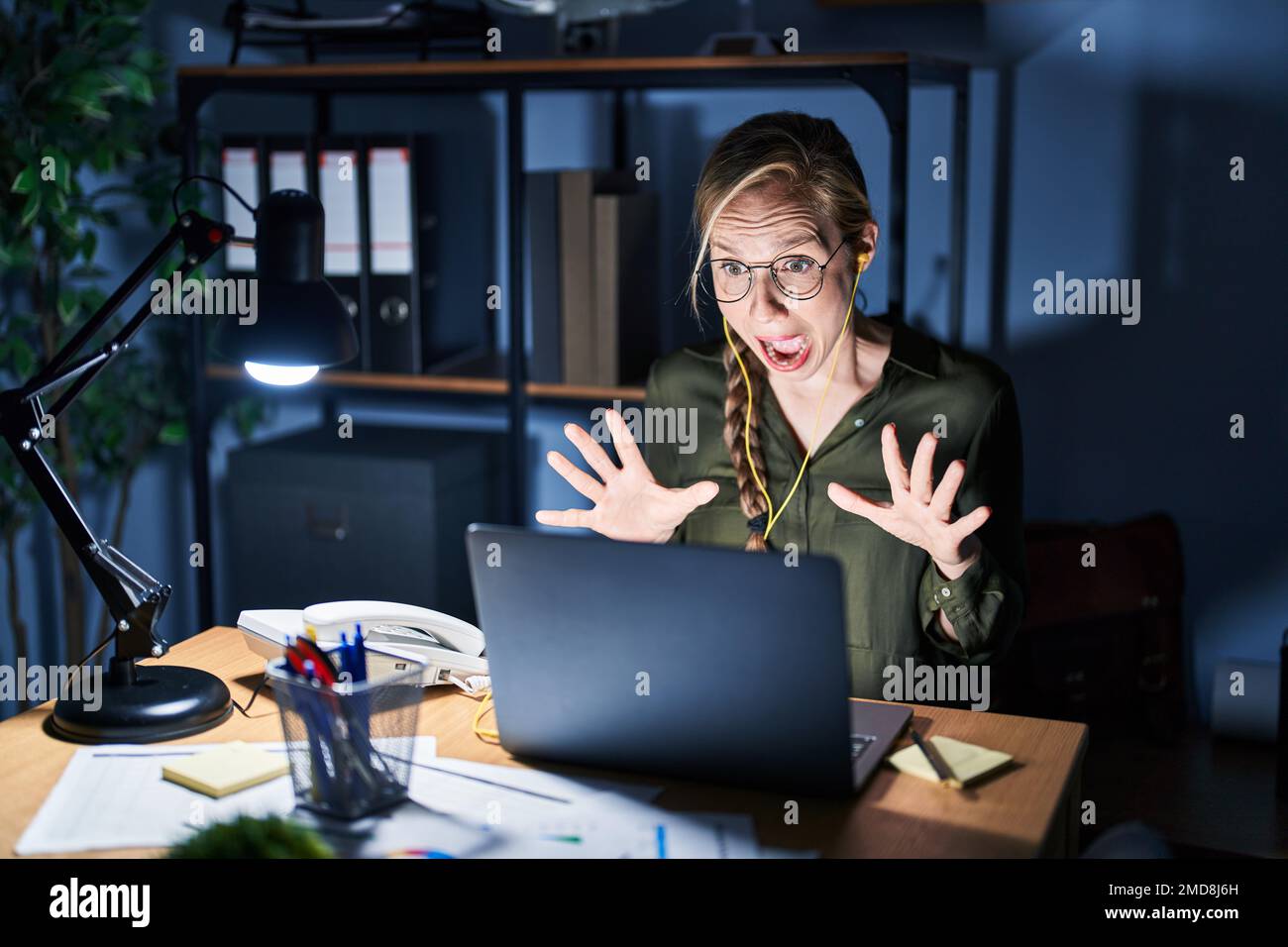 Young blonde woman working at the office at night afraid and terrified ...