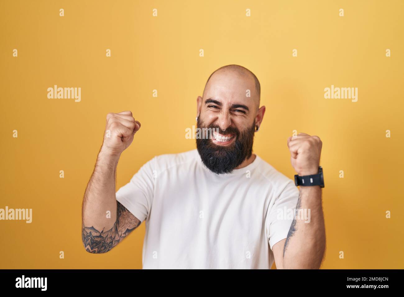 Young hispanic man with beard and tattoos standing over yellow ...