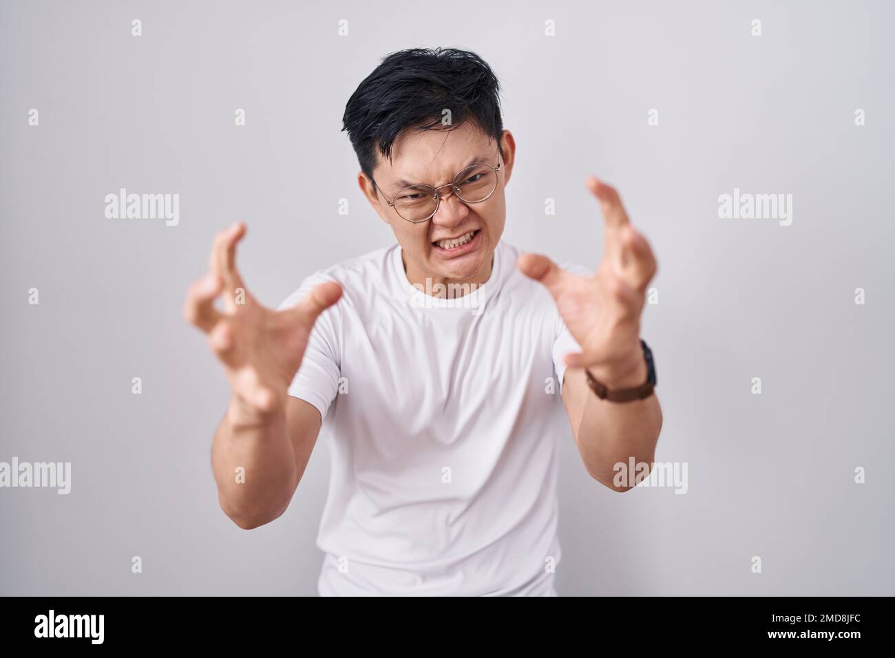 Young asian man standing over white background shouting frustrated with ...