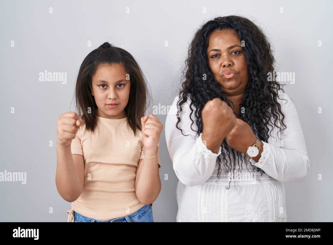 Mother and young daughter standing over white background ready to fight ...