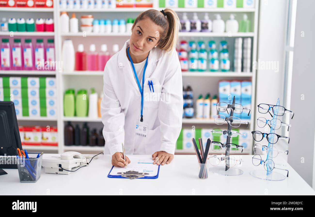 Young beautiful hispanic woman pharmacist smiling confident writing on ...