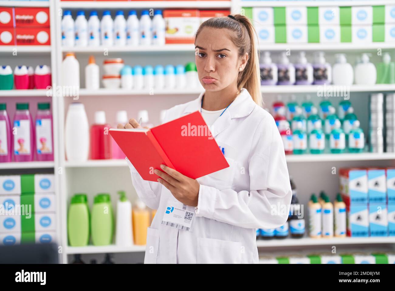 Young blonde woman working at pharmacy drugstore holding notebook ...