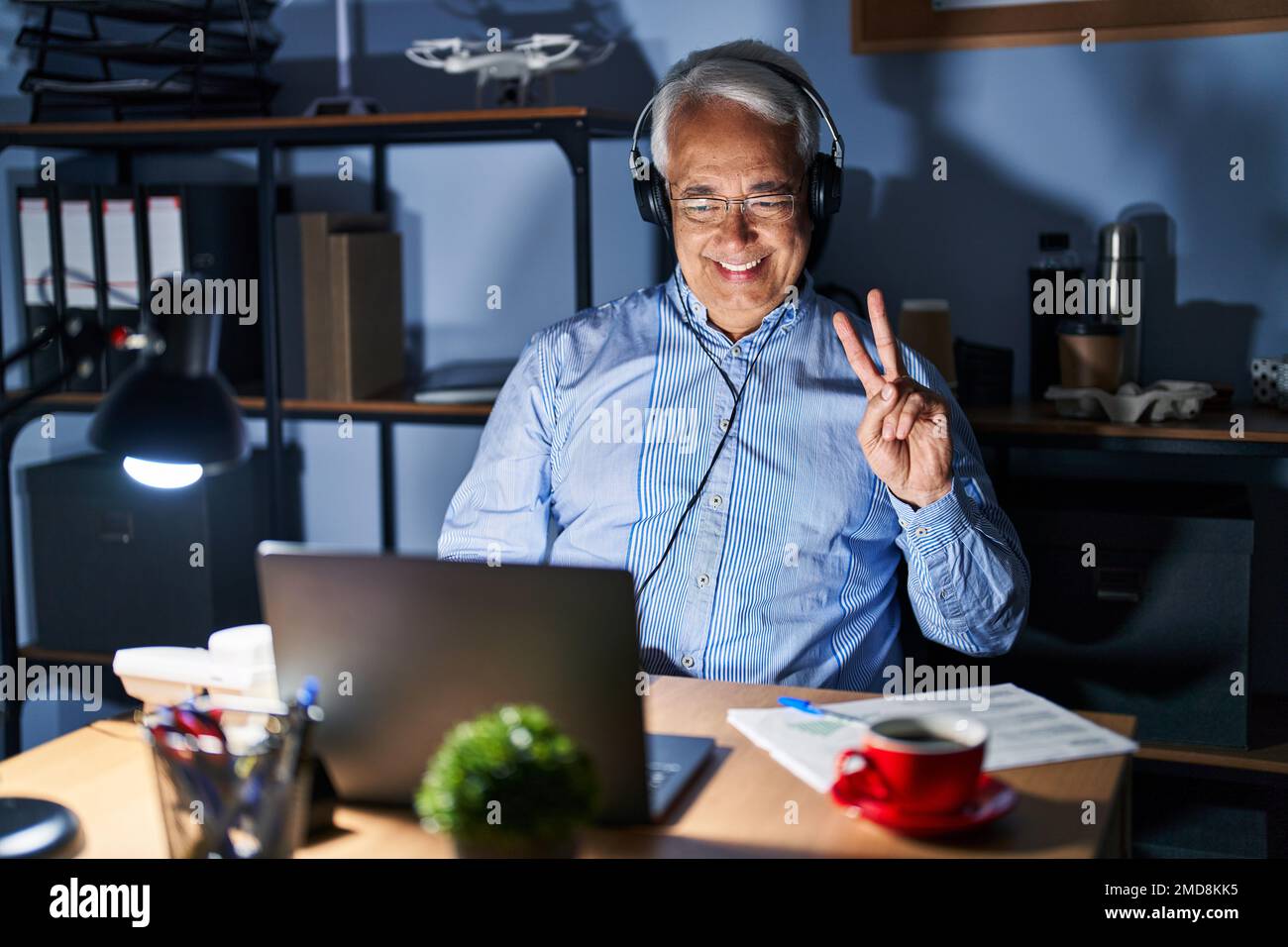 Hispanic senior man wearing call center agent headset at night smiling ...