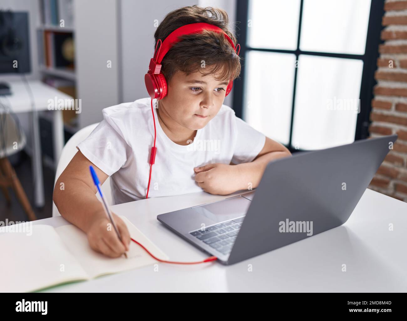 Adorable hispanic boy student using laptop writing on notebook at ...