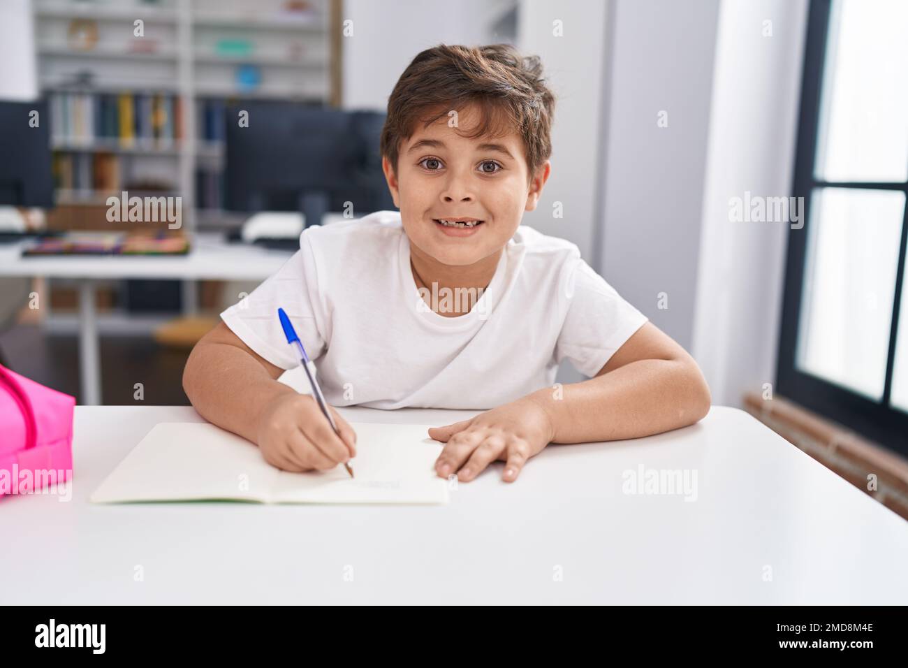 Adorable hispanic boy student smiling confident writing on notebook at ...