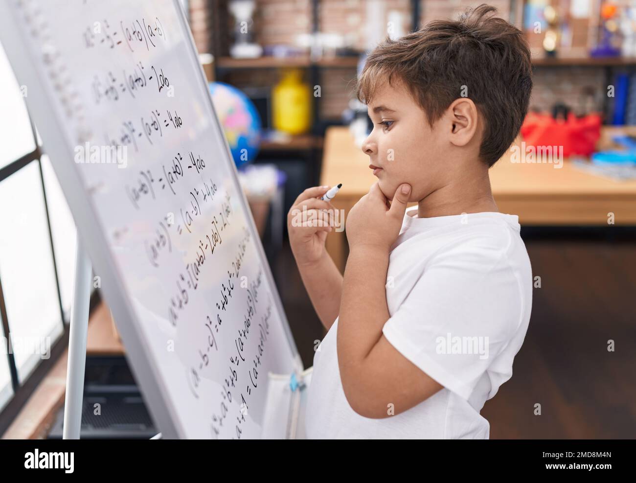 Adorable hispanic boy preschool student writing on chalkboard at ...