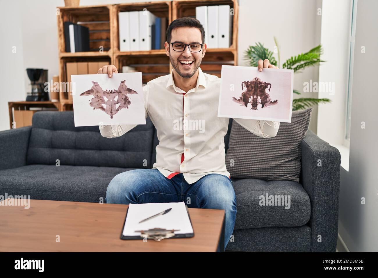 Young hispanic man with beard holding rorschach test smiling and ...