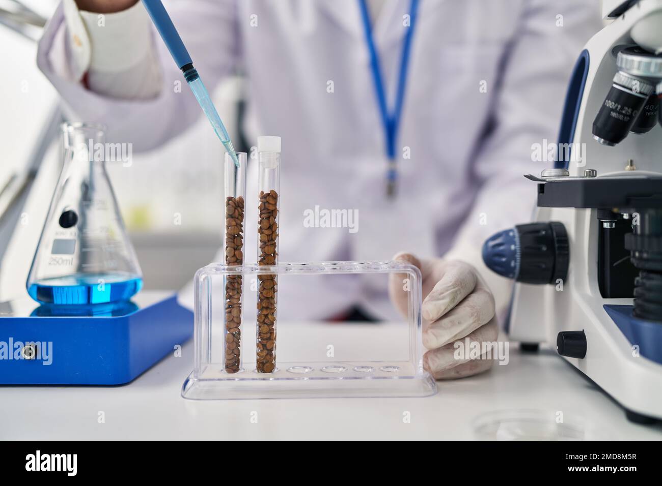Young hispanic man scientist using pipette pouring liquid at laboratory ...