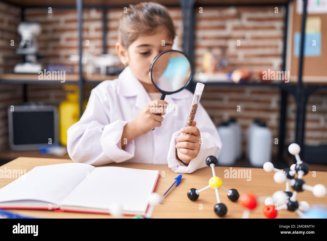 Adorable hispanic girl student looking test tube using magnifying glass ...