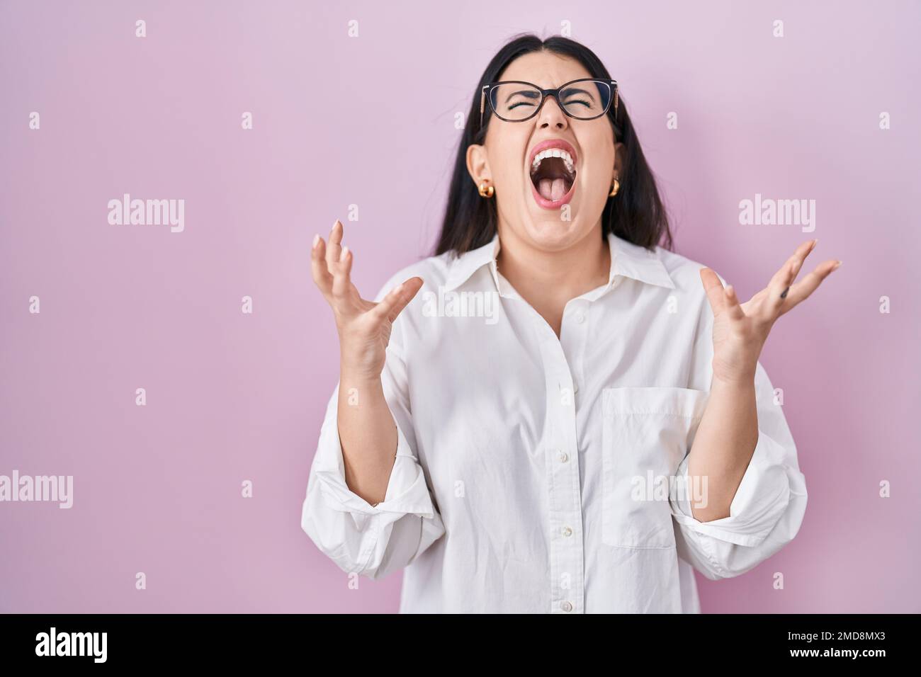 Young brunette woman standing over pink background crazy and mad ...