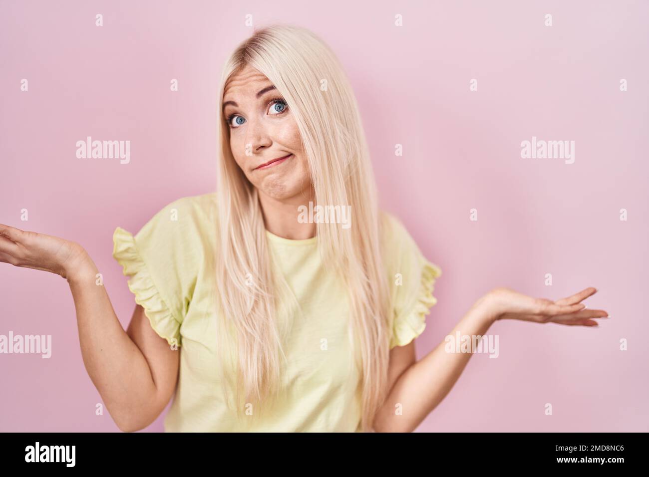 Caucasian woman standing over pink background clueless and confused ...