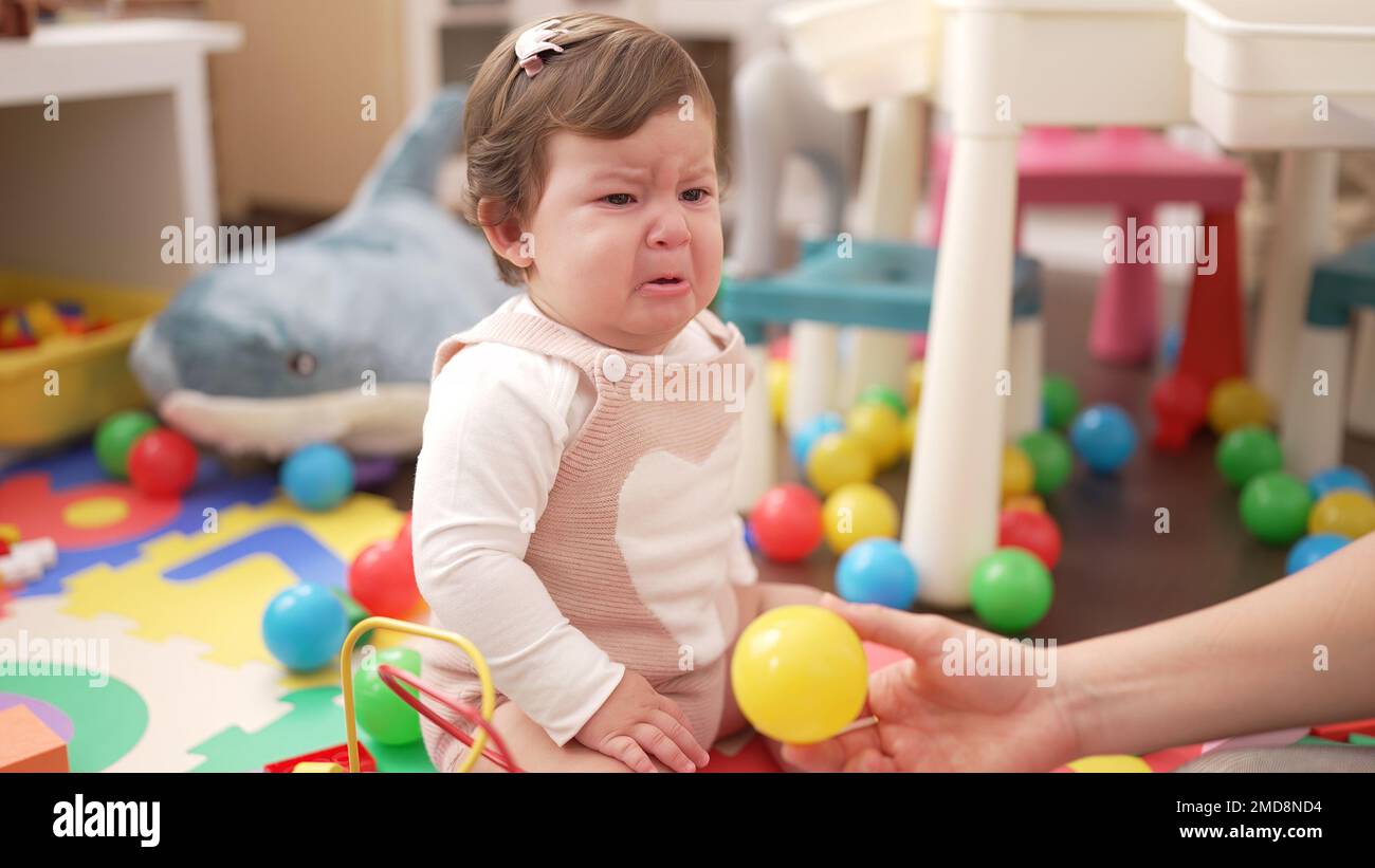 Adorable toddler sitting on floor looking ball crying at kindergarten ...