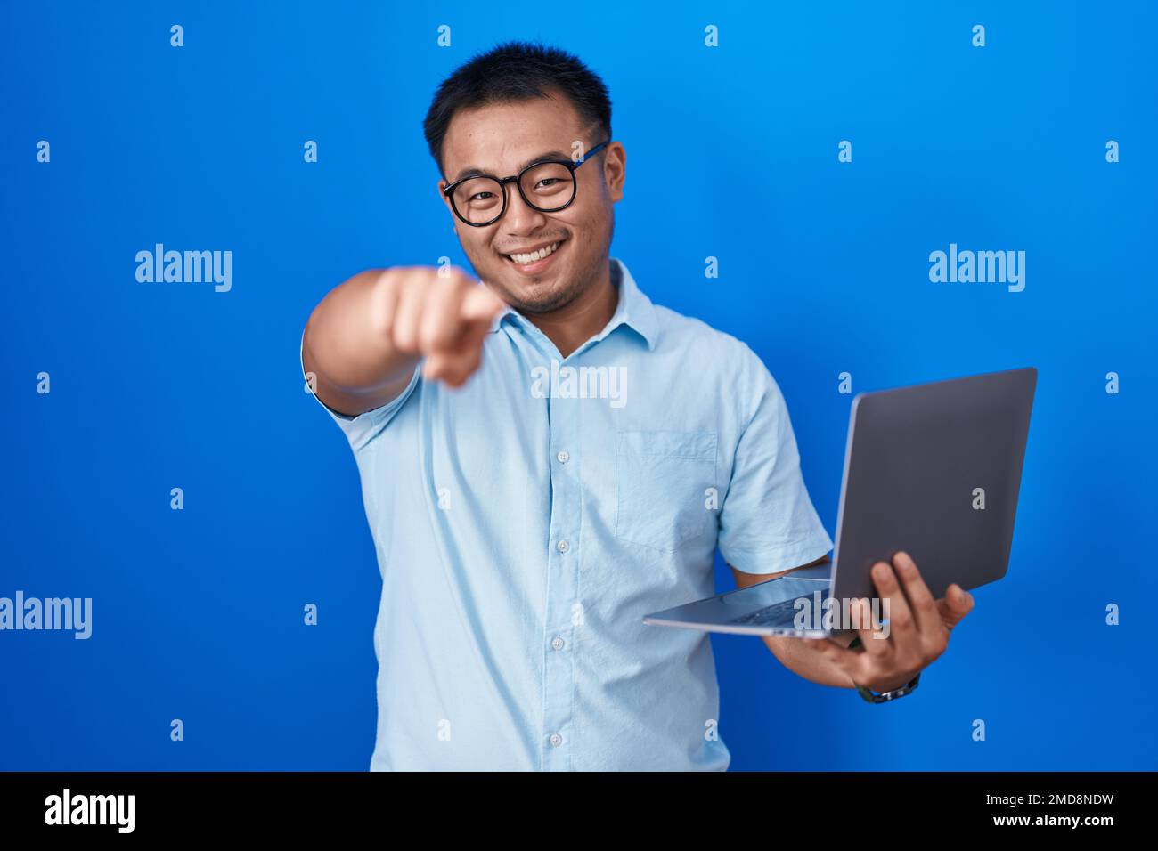 Chinese young man using computer laptop pointing to you and the camera ...