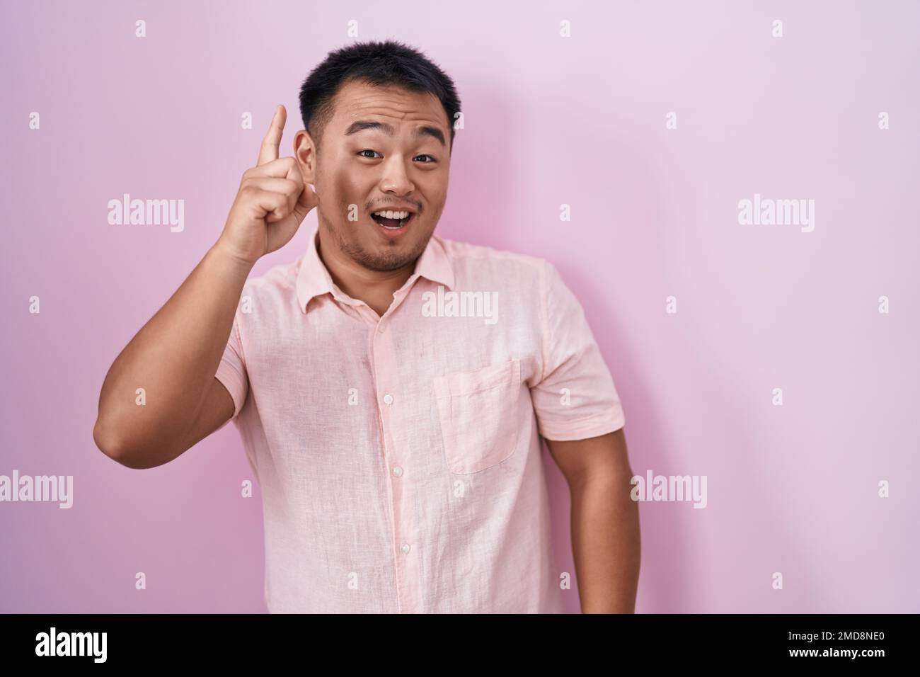 Chinese young man standing over pink background pointing finger up with ...
