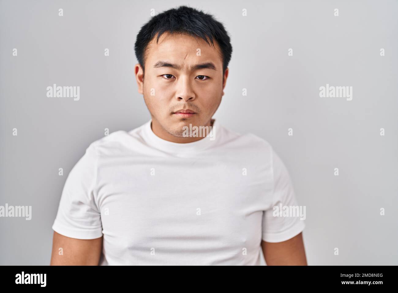 Young chinese man standing over white background skeptic and nervous, frowning upset because of ...