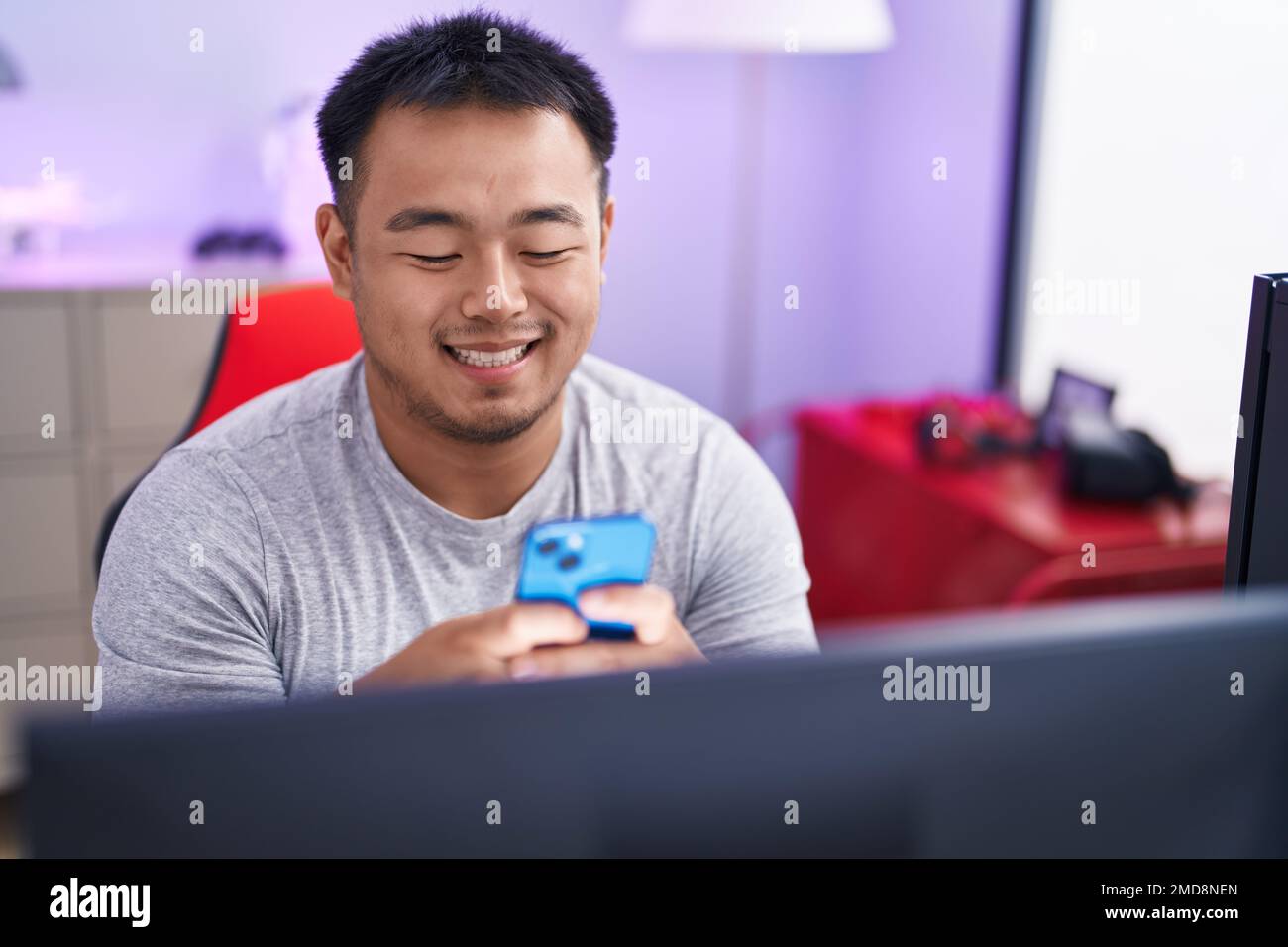 Young chinese man streamer using computer and smartphone at gaming room ...