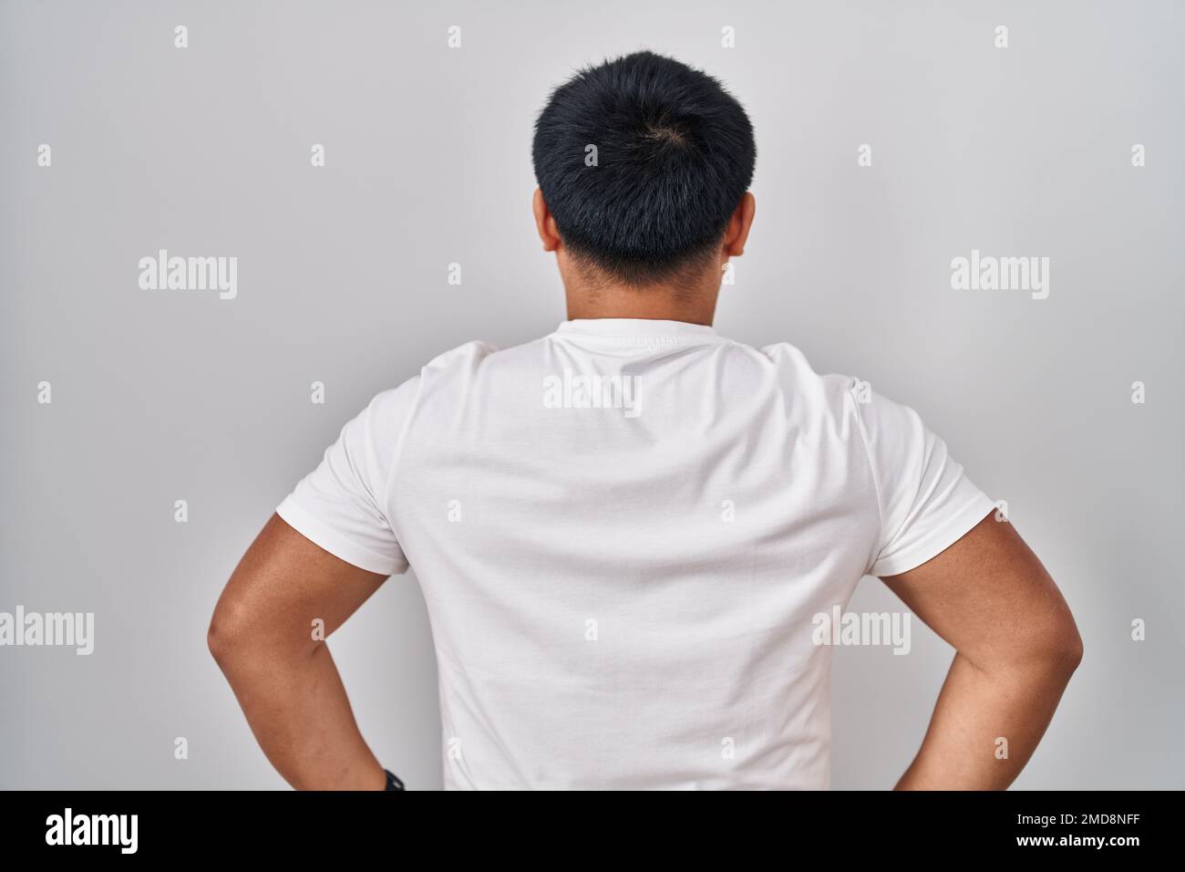 Young chinese man standing over white background standing backwards ...