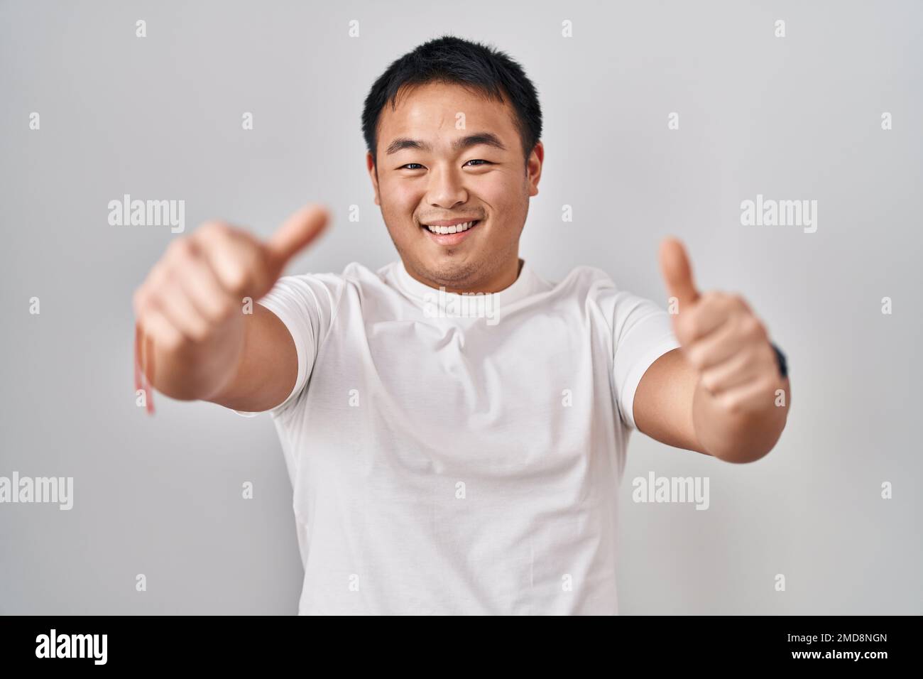 Young chinese man standing over white background approving doing ...