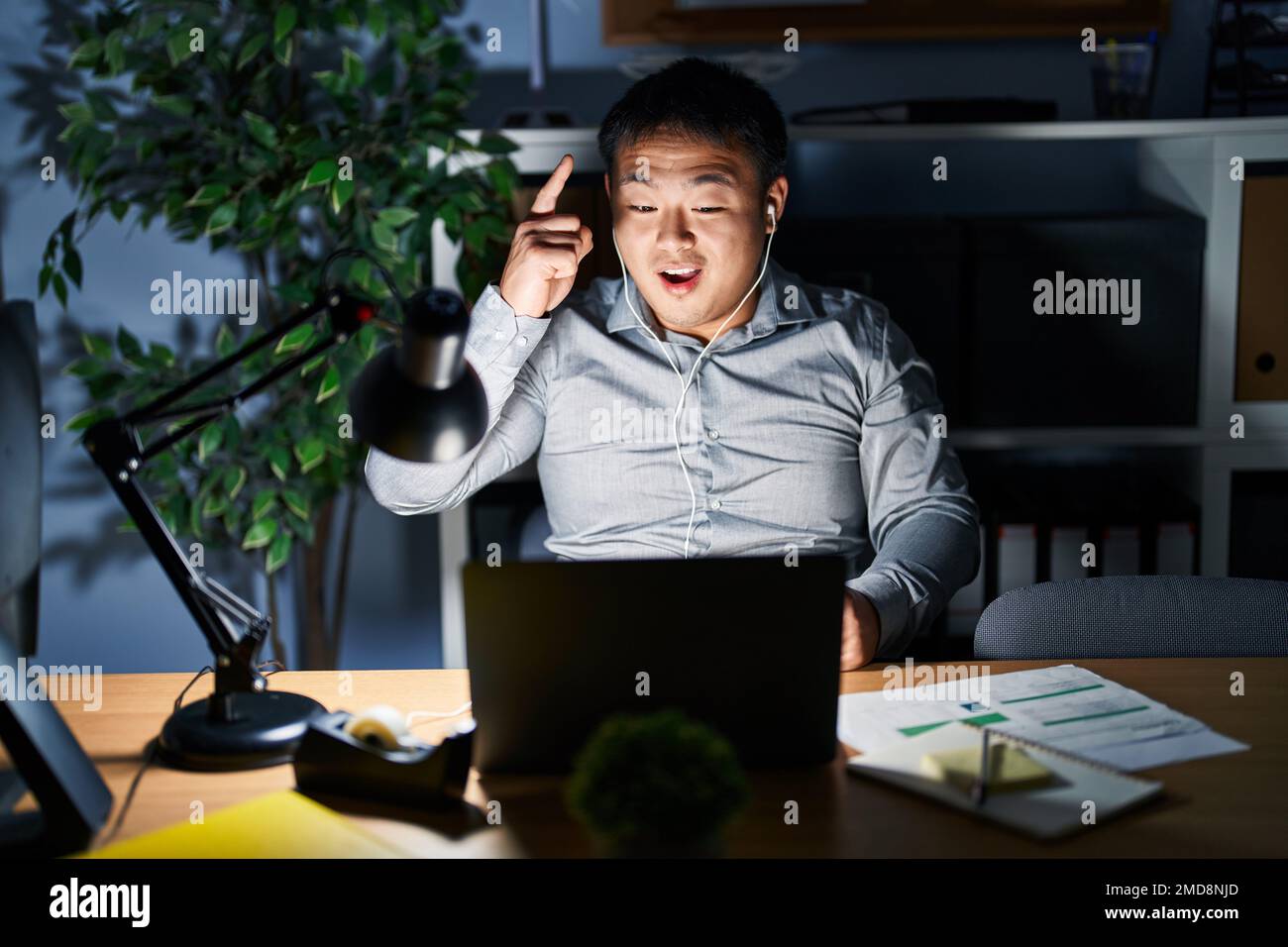 Young chinese man working using computer laptop at night pointing ...