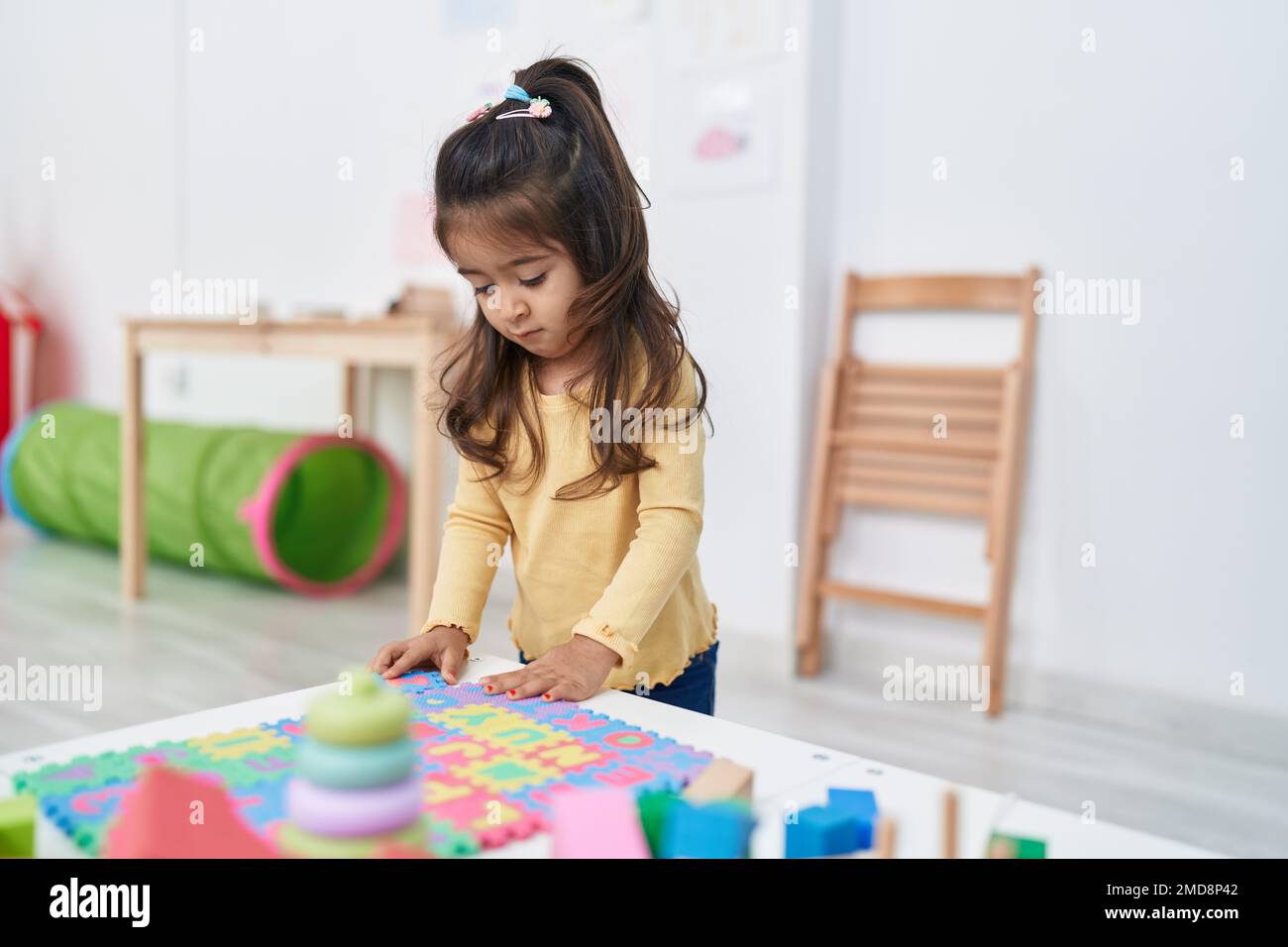Adorable hispanic girl playing with game standing at kindergarten Stock ...
