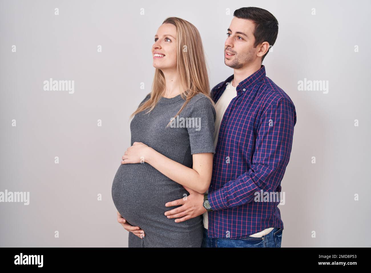 Young couple expecting a baby standing over white background looking to ...