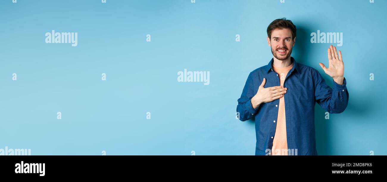 Honest young man smiling and making promise, holding hand on heart and ...