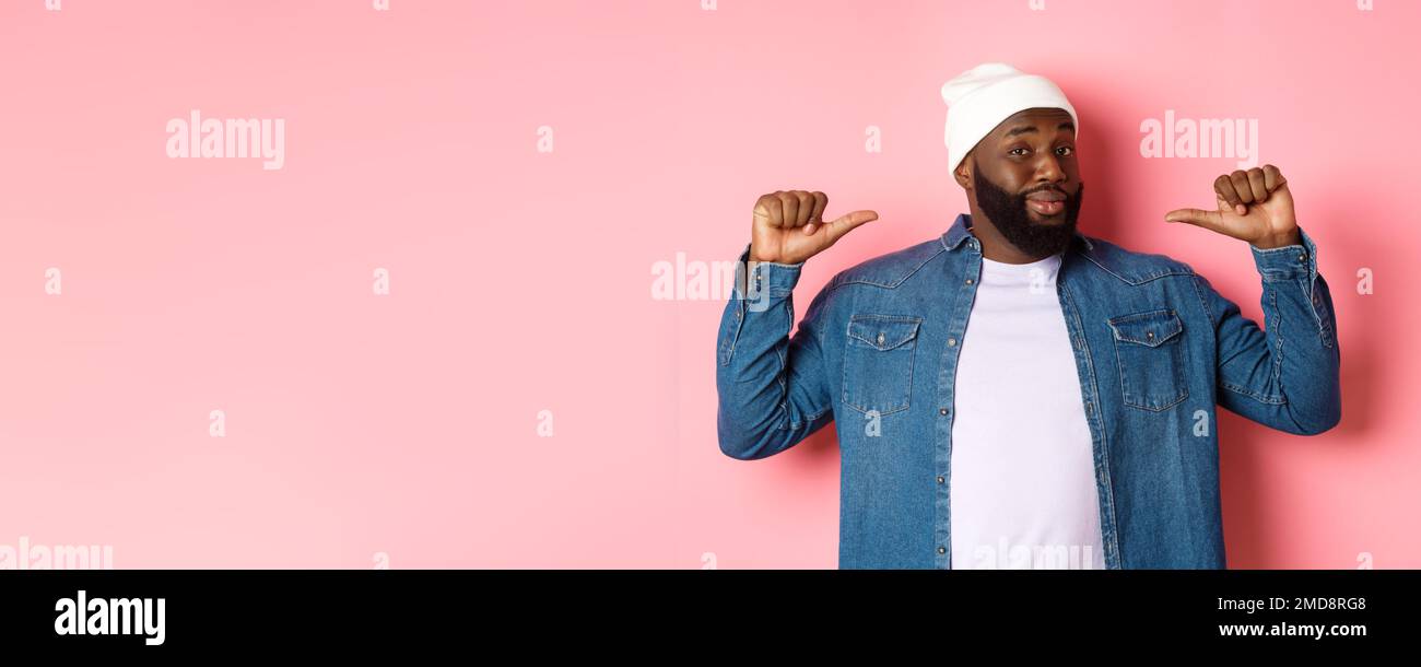 Confident and cheeky Black man pointing at himself, staring at camera ...