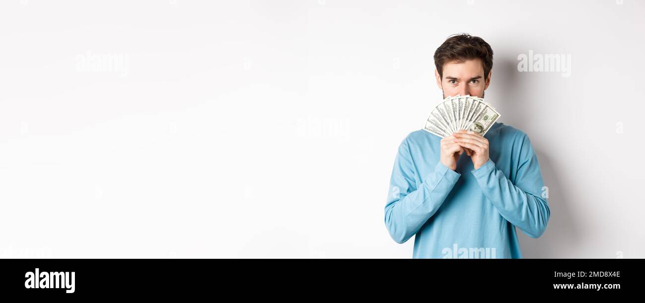 Finance concept. Smiling young man covering face behind money, showing ...
