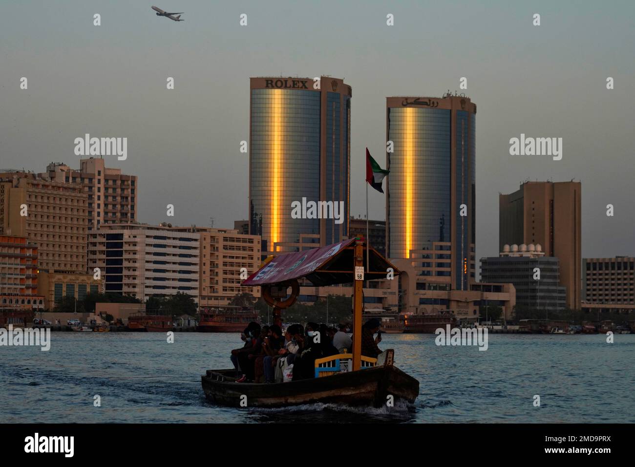 A traditional abra boat traverses the Dubai Creek at sunset as a plane ...