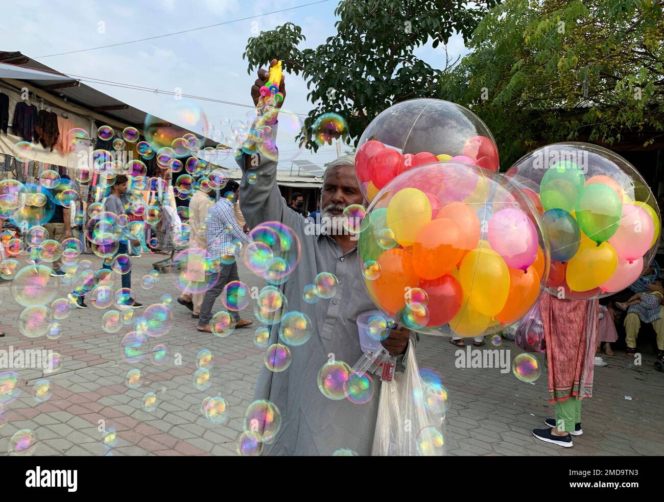 A Pakistani balloon vendor makes bubbles to attract customers at a ...