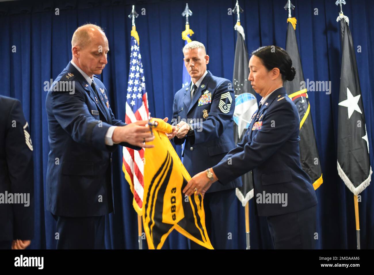 Col. Mia Walsh, commander, Space Base Delta 3, right, unfurls the SBD 3 ...